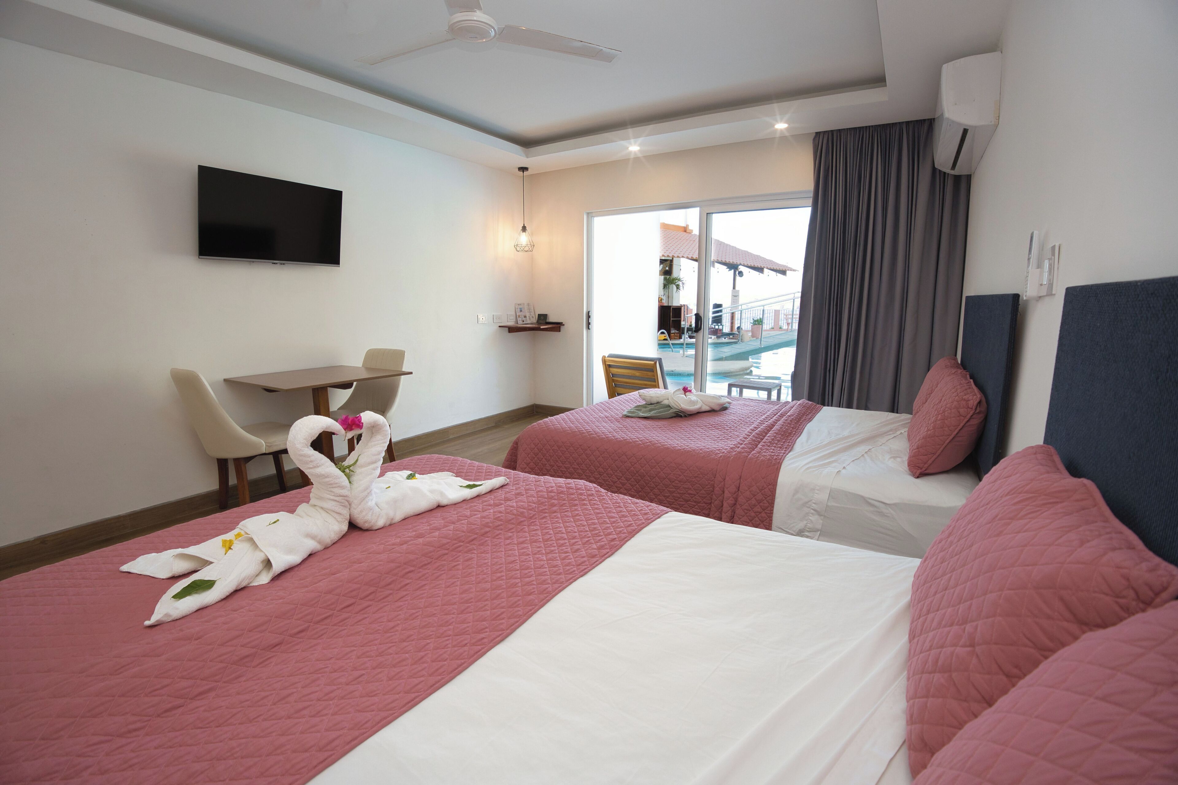 Quarto de hotel com duas camas, uma escrivaninha, televisão e vista para uma piscina.