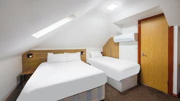 Quarto de hotel com duas camas, cabeceira de madeira, ar condicionado integrado e porta com moldura de madeira.