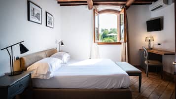 Quarto com cama, mesas de cabeceira, escrivaninha, cadeira, televisão e janela com vista para o verde.