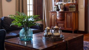 Uma mesa de centro de madeira com um vaso azul e bules de prata, um sofá de couro e um aparador de madeira com um espelho e objetos decorativos.