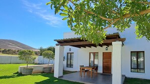 Uma casa moderna com um alpendre, uma mesa de madeira e uma pequena árvore.