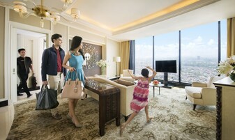 Quarto de hotel com uma grande janela, um sofá, uma televisão e um detalhe decorativo na parede.