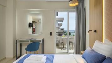 Quarto de hotel com cama, escrivaninha, cadeira, varanda com mesa e cadeiras, e vista para o mar.