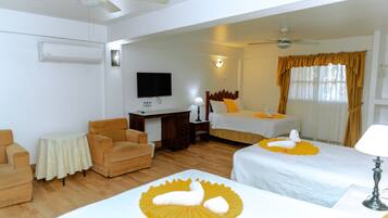 Quarto de hotel com duas camas, uma escrivaninha, uma cadeira, uma televisão e um ventilador de teto.