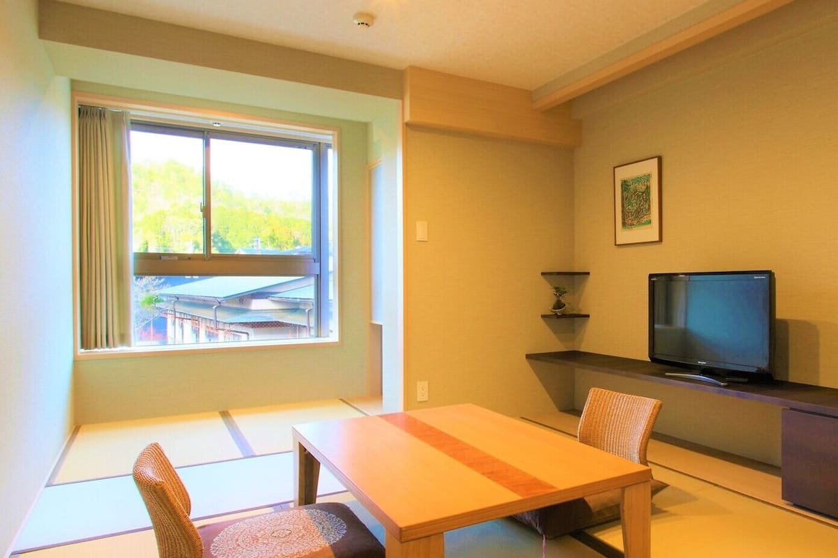 Quarto com esteiras de tatame, uma mesa baixa, televisão e janela com cortinas.