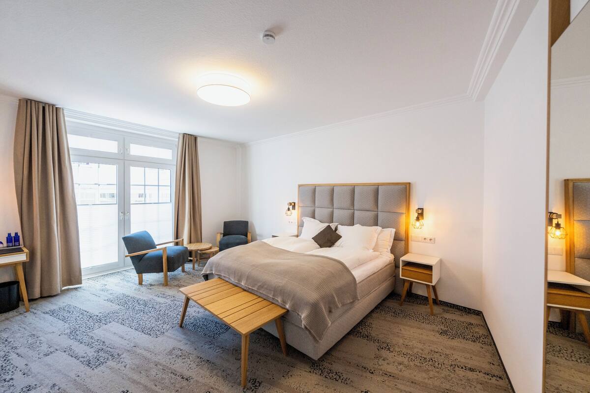Quarto de hotel com uma cama grande, uma mesa, uma cadeira e uma mesinha.