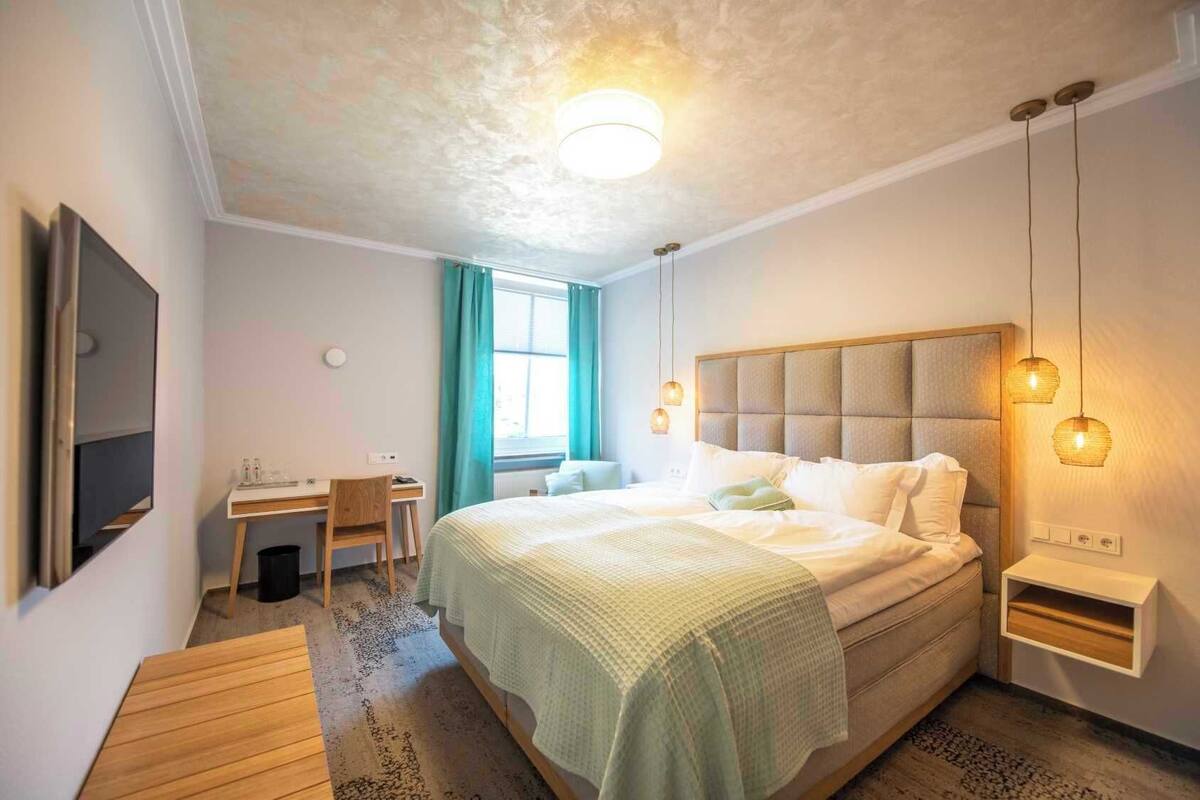 Quarto de hotel com cama, escrivaninha, cadeira e vista para o exterior.