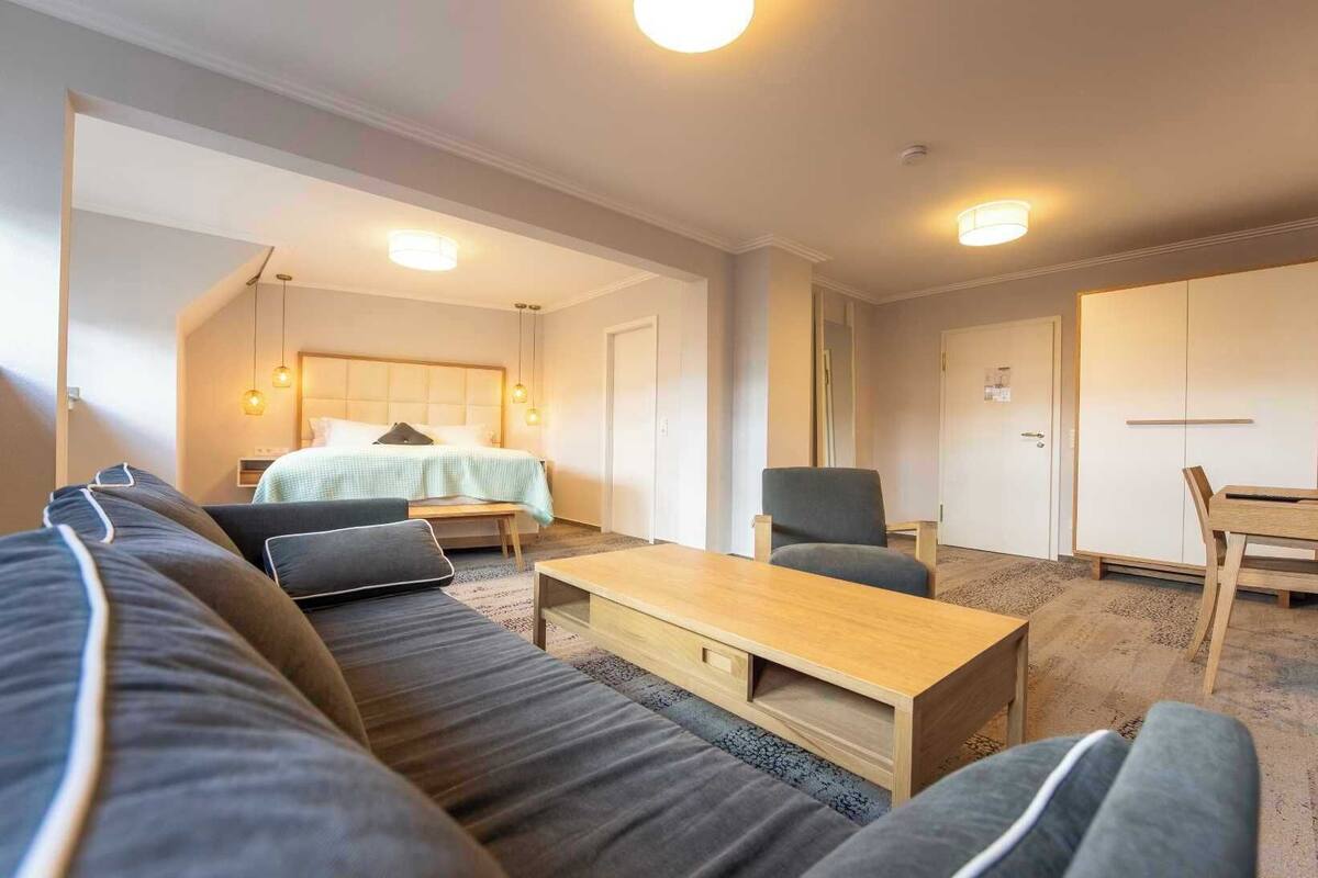Quarto de hotel moderno com sofá, mesa de centro de madeira, escrivaninha e cama com cabeceira.
