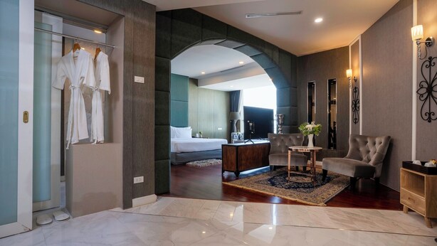 Quarto de hotel moderno com piso de mármore, uma cama, área de estar com mesa e cadeiras, e banheiro com chuveiro e porta-toalhas.