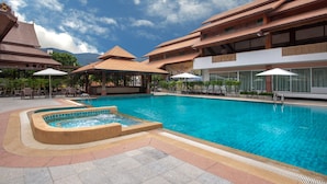 Piscina com hidromassagem, rodeada por espreguiçadeiras e guarda-sóis, com edifícios tradicionais e modernos ao fundo.