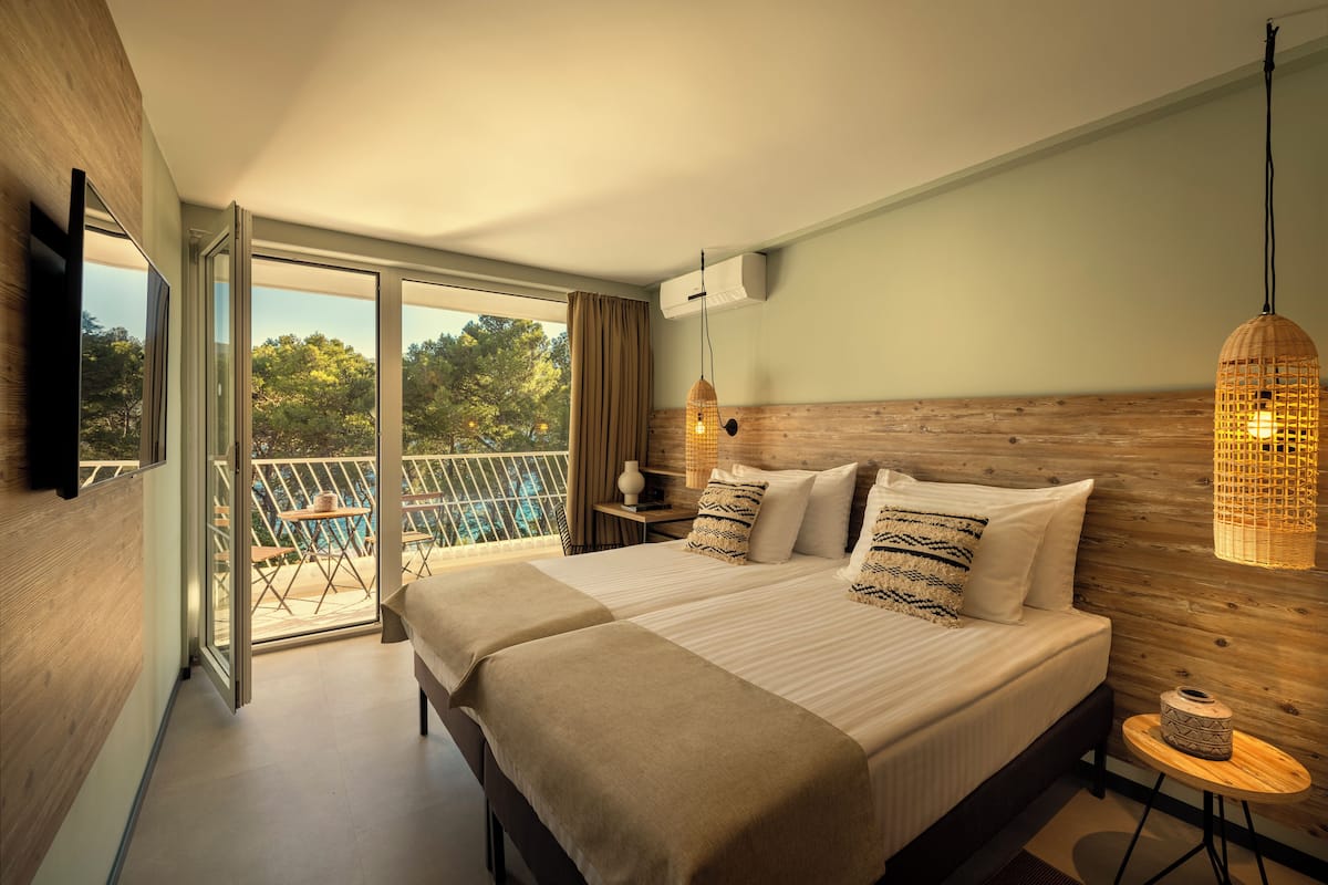 Quarto de hotel moderno com uma cama grande, varanda com vista e televisão de tela plana na parede.