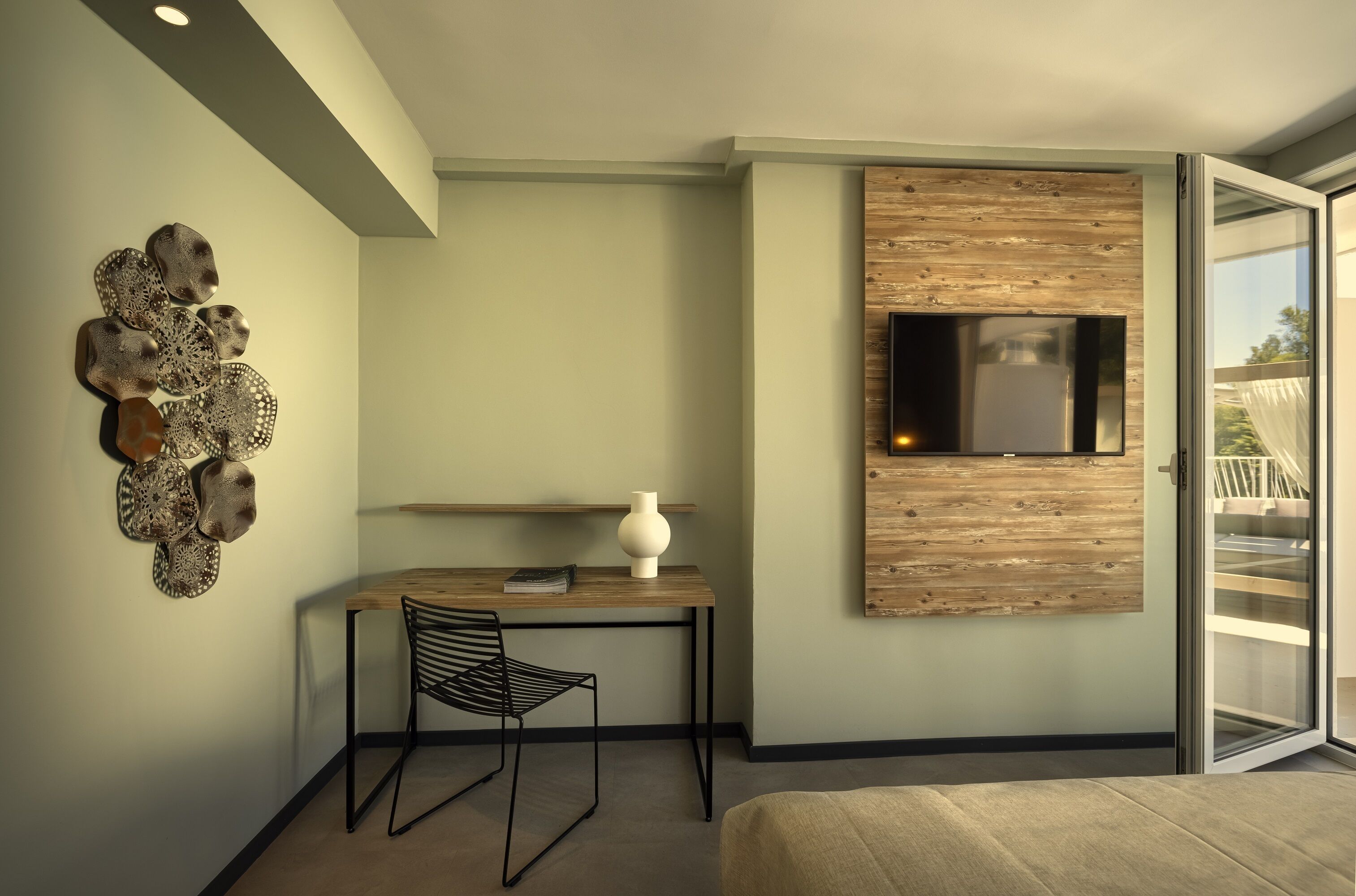Quarto moderno com escrivaninha, cadeira e TV fixada numa parede revestida de madeira.