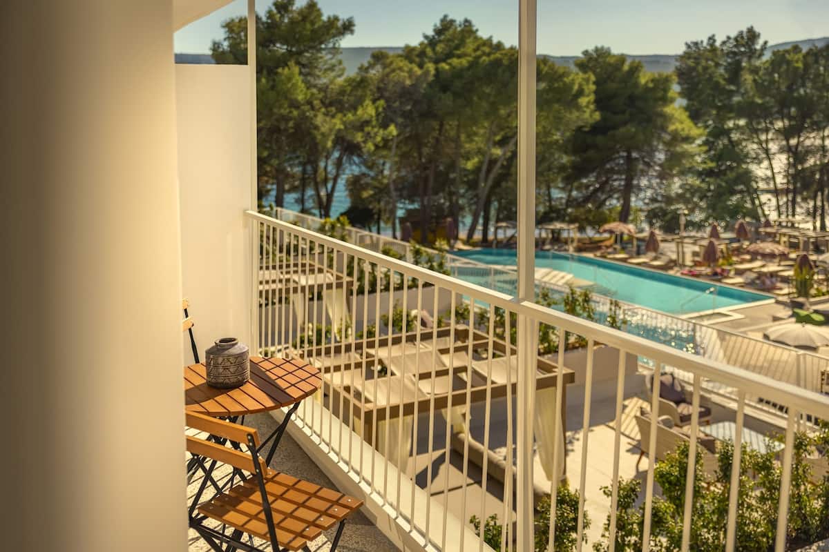 Varanda com vista para uma piscina e área de lazer, incluindo espreguiçadeiras e guarda-sóis.