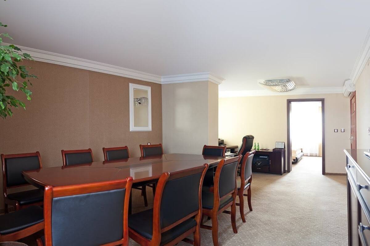 Uma sala de conferências com uma mesa comprida e cadeiras, uma televisão e uma planta.