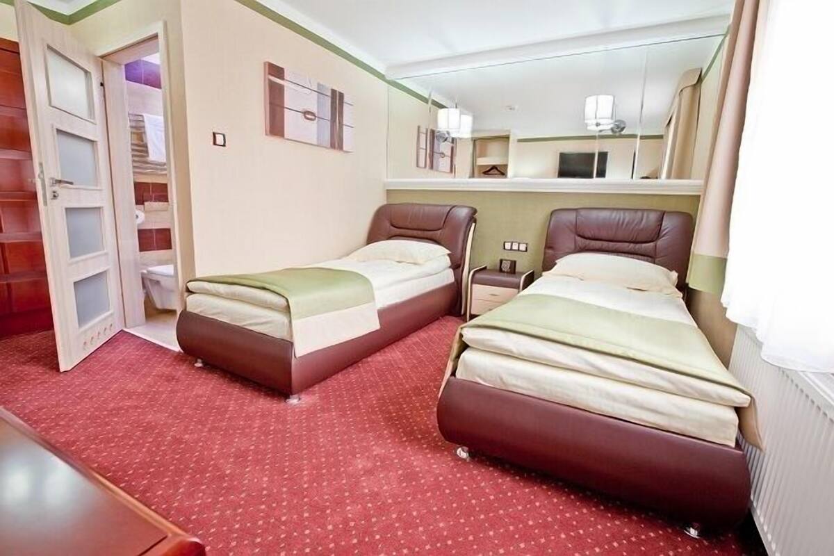 Quarto de hotel com duas camas, uma mesa pequena, um guarda-roupa e um espelho.
