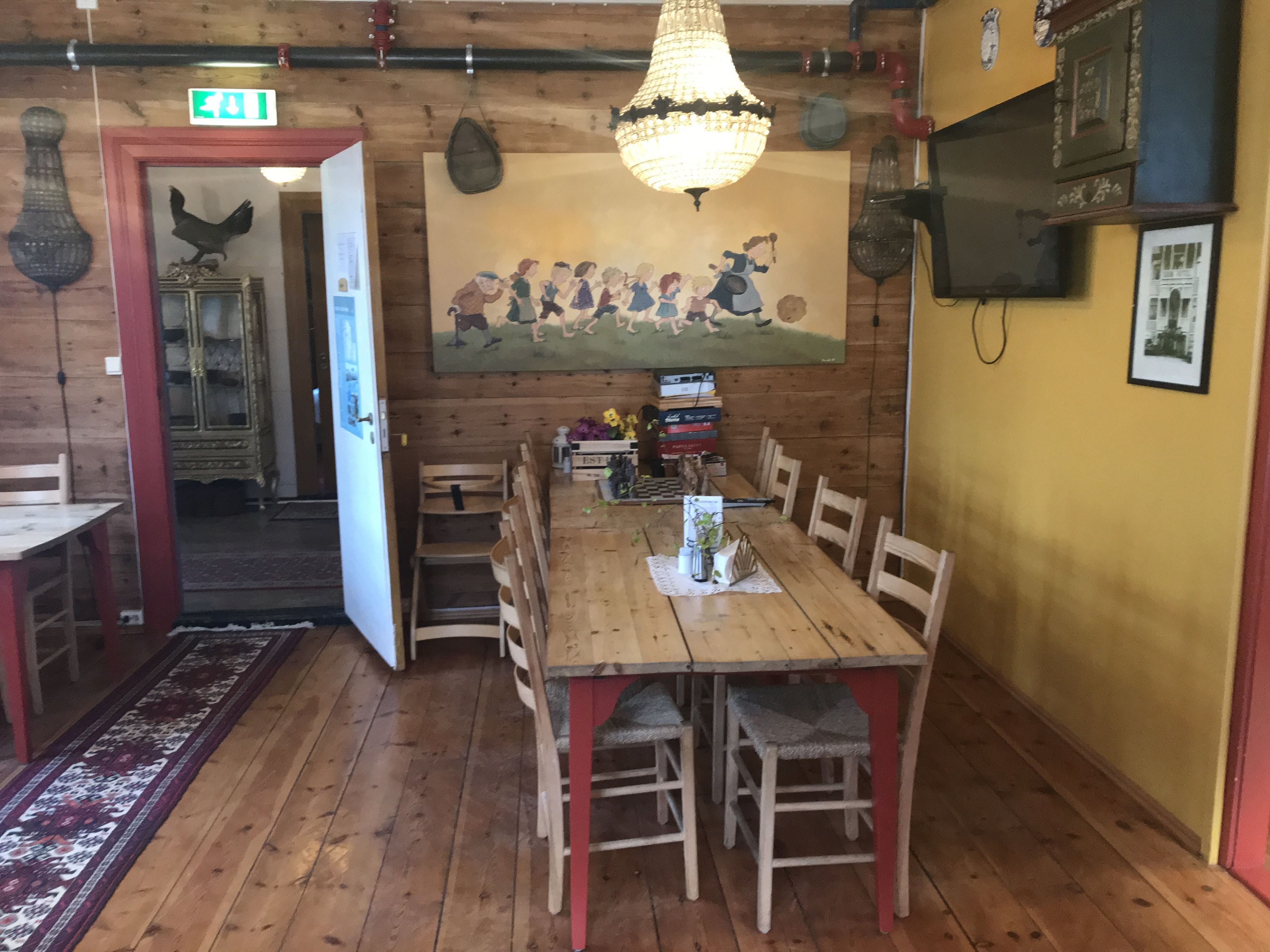 Um restaurante com mesas e cadeiras de madeira, um candelabro e um quadro na parede.