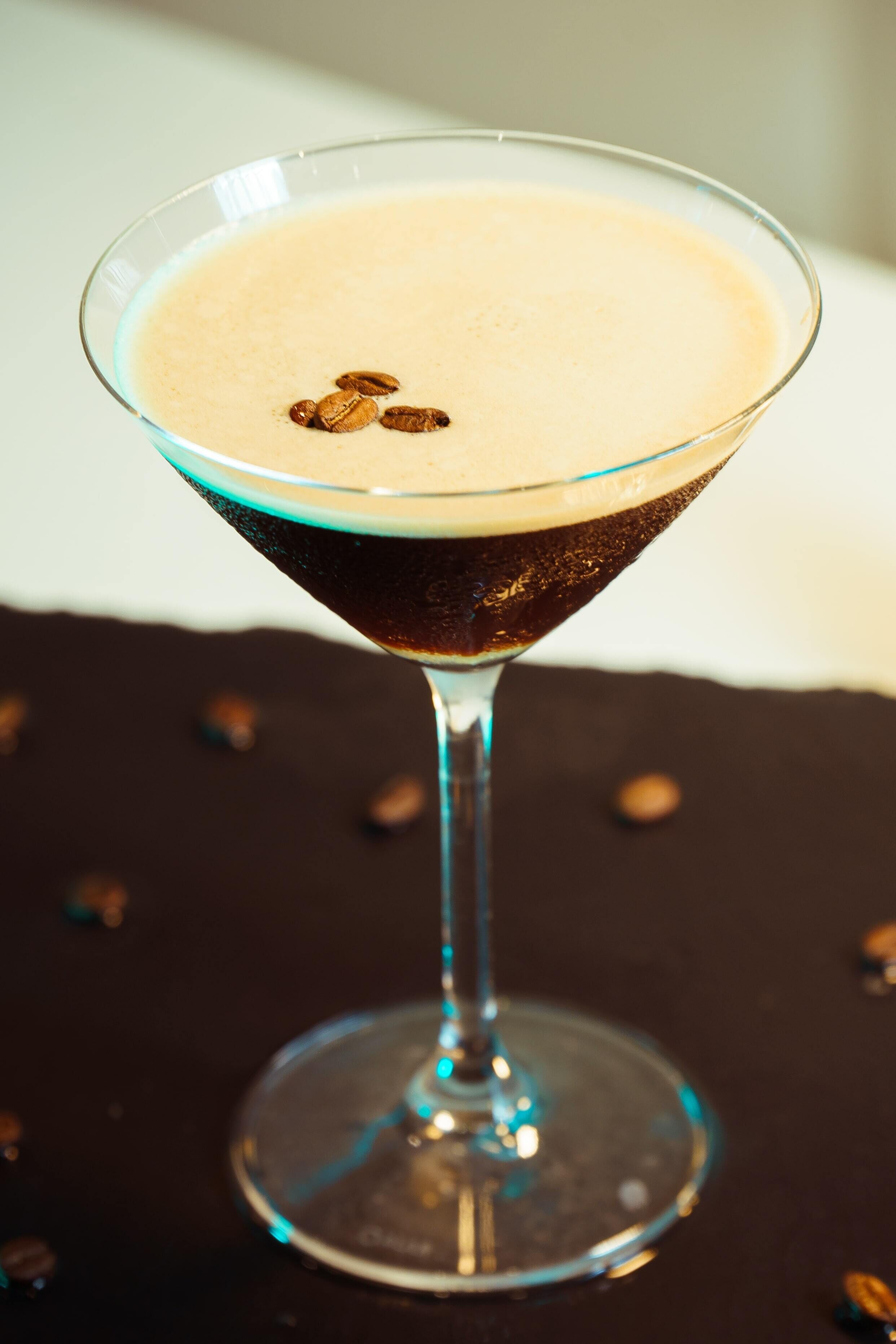 Um copo de martini com uma bebida em camadas, apoiado sobre uma superfície escura com nozes espalhadas.
