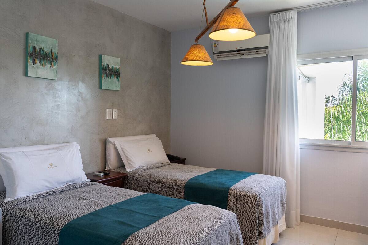 Quarto com duas camas, janela com cortinas e duas pinturas penduradas na parede.
