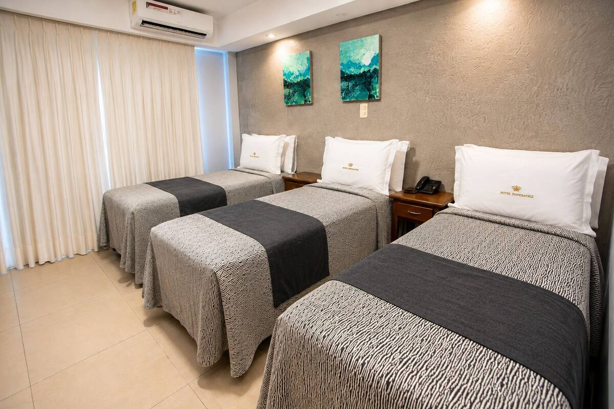 Quarto de hotel com três camas, uma mesa de cabeceira com telefone e obras de arte na parede.