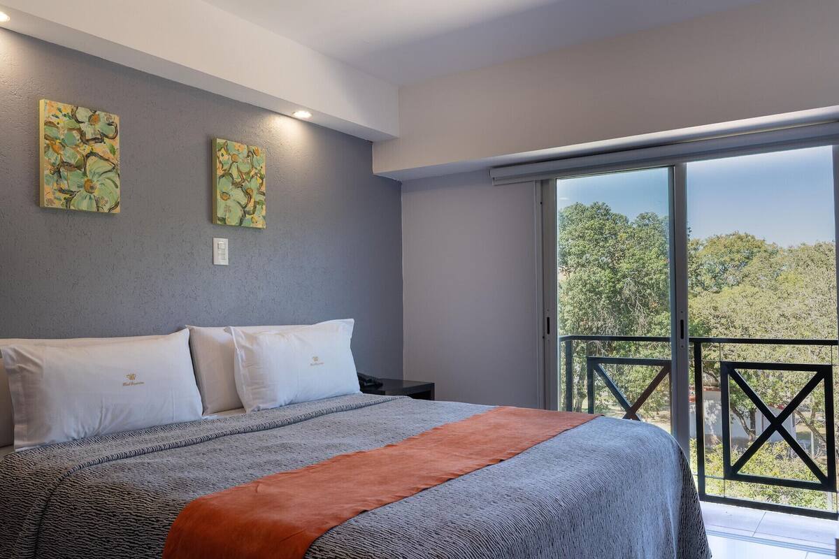 Quarto com uma cama, duas pinturas e uma varanda com vista para árvores.