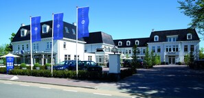 Um hotel com estilo arquitetônico europeu tradicional, destacando uma entrada imponente, várias janelas e um acesso bem cuidado.