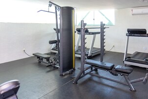 Academia com equipamentos de ginástica, esteira e banco.