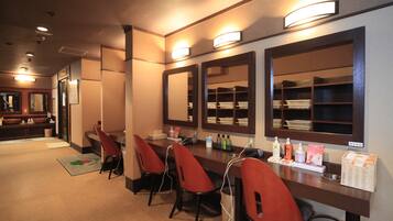 Quarto de hotel com área de jantar, destacando uma mesa comprida, cadeiras vermelhas e um espelho sobre a mesa.