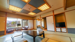 Um quarto japonês tradicional com tatames, uma mesa baixa e uma televisão.