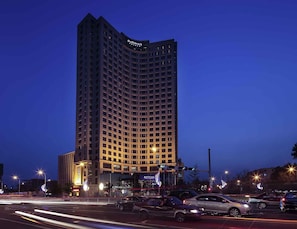 Um hotel moderno de vários andares com fachada curva, janelas iluminadas e uma placa 'Pullman' bem visível no topo.