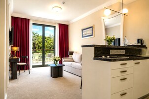Quarto de hotel moderno com varanda, sofá, mesa de jantar e área de cozinha.
