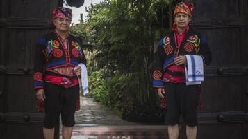 Duas pessoas vestidas com trajes típicos em frente a um arco de madeira, com uma passagem visível.