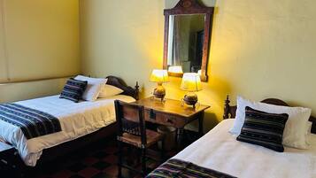Quarto com duas camas, uma escrivaninha de madeira, duas luminárias e um espelho na parede.