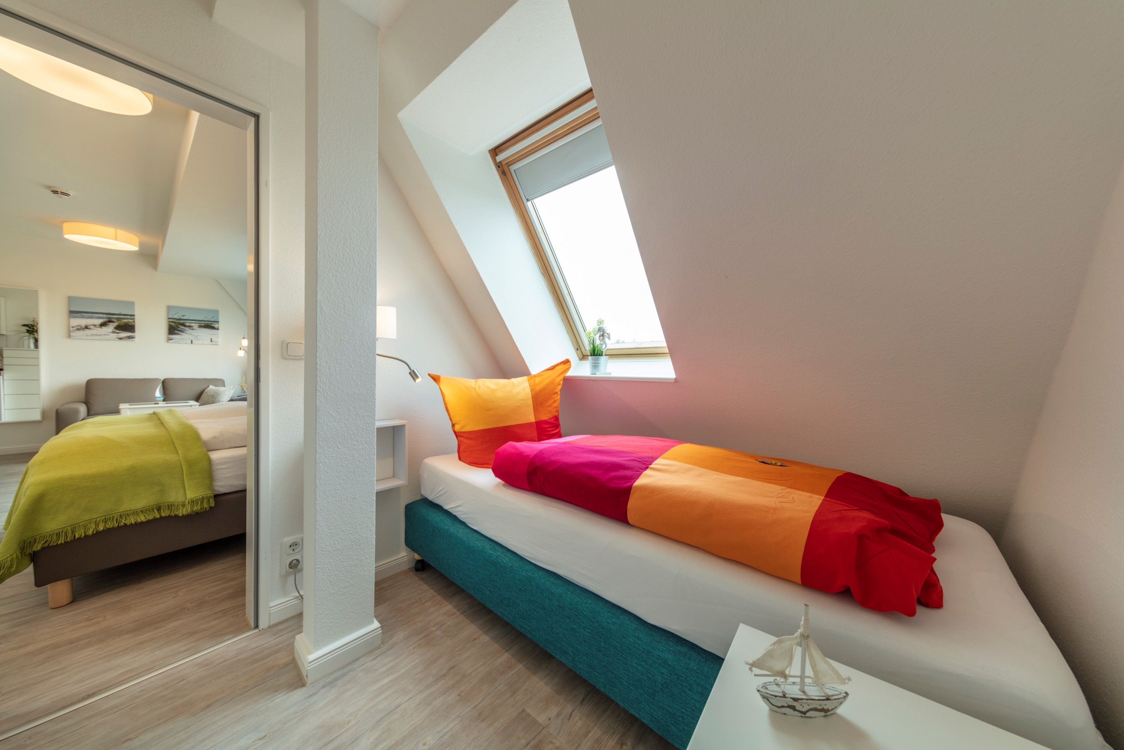 Quarto moderno com claraboia, cama com roupa de cama colorida e um pequeno modelo de navio na mesa de cabeceira.