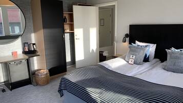 Quarto de hotel moderno com uma cama grande, um guarda-roupa, uma pequena escrivaninha e um espelho.