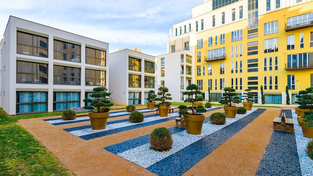 Um pátio com edifícios modernos, plantas em vasos e um caminho de cascalho.