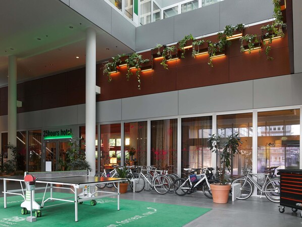 Um hall de hotel com mesa de pingue-pongue, bicicletas e um tapete verde com uma mensagem.