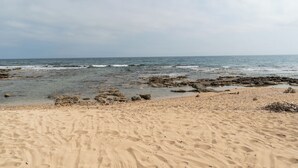 Uma praia arenosa com pegadas visíveis e pedras espalhadas.