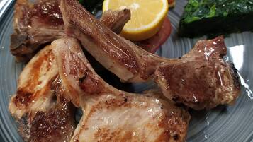 Um prato com carne grelhada, vegetais e uma fatia de limão.