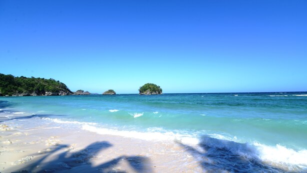 Uma praia com águas turquesa cristalinas, areia branca e ilhas verdes ao longe.