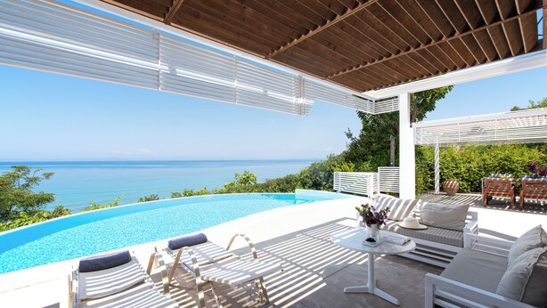 Área da piscina com espreguiçadeiras, uma mesa com um vaso de flores e vista para o mar.