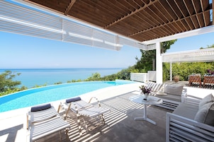Área da piscina com espreguiçadeiras, uma mesa com um vaso de flores e vista para o mar.
