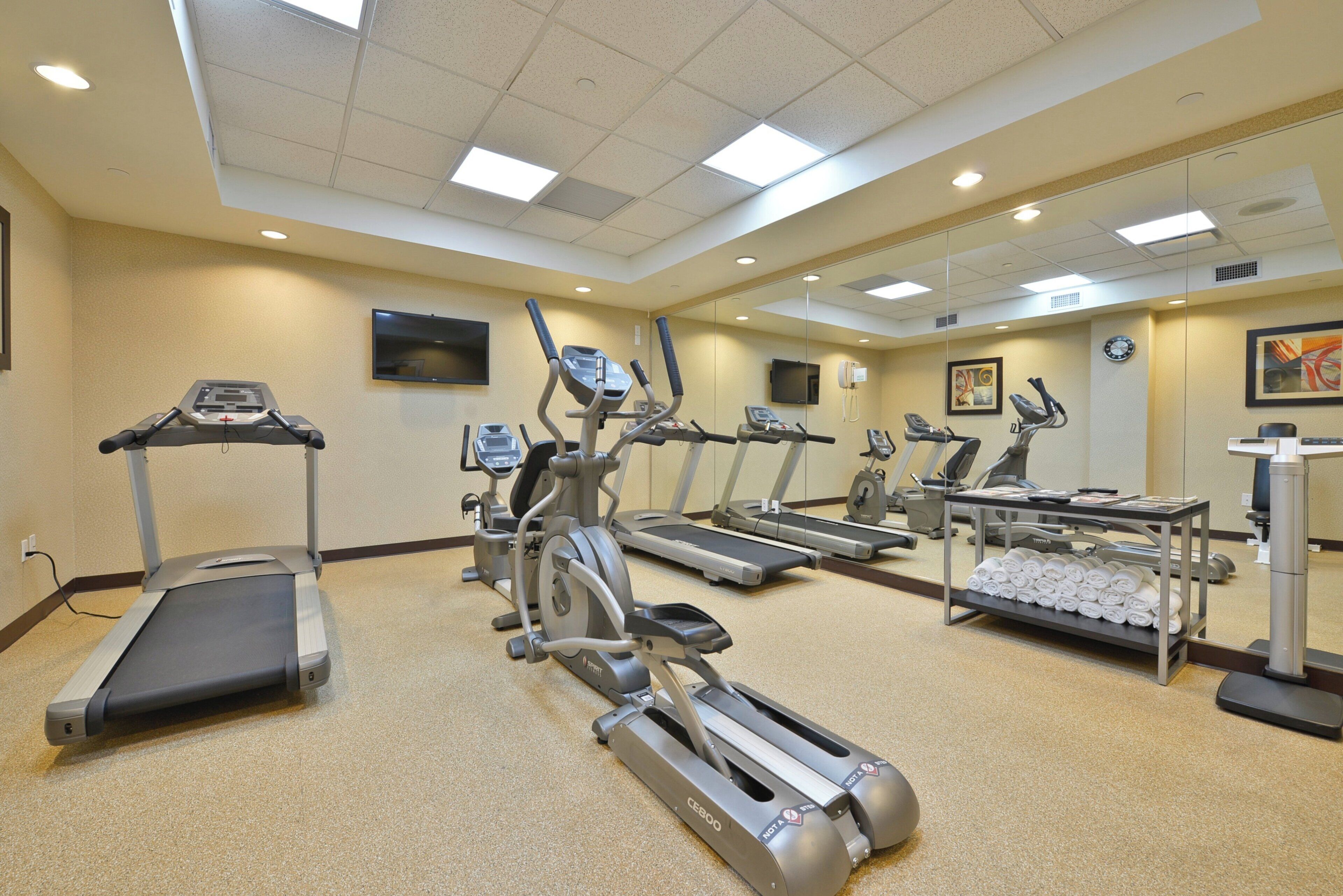 Centro de fitness com esteiras, elípticos e um espelho grande.