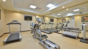 Centro de fitness com esteiras, elípticos e um espelho grande.