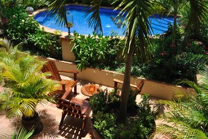 Piscina rodeada por vegetação exuberante, móveis de madeira e um muro de pedra.