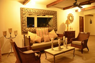 Uma sala de estar aconchegante com um sofá, duas poltronas, uma mesa de centro e um espelho decorativo.