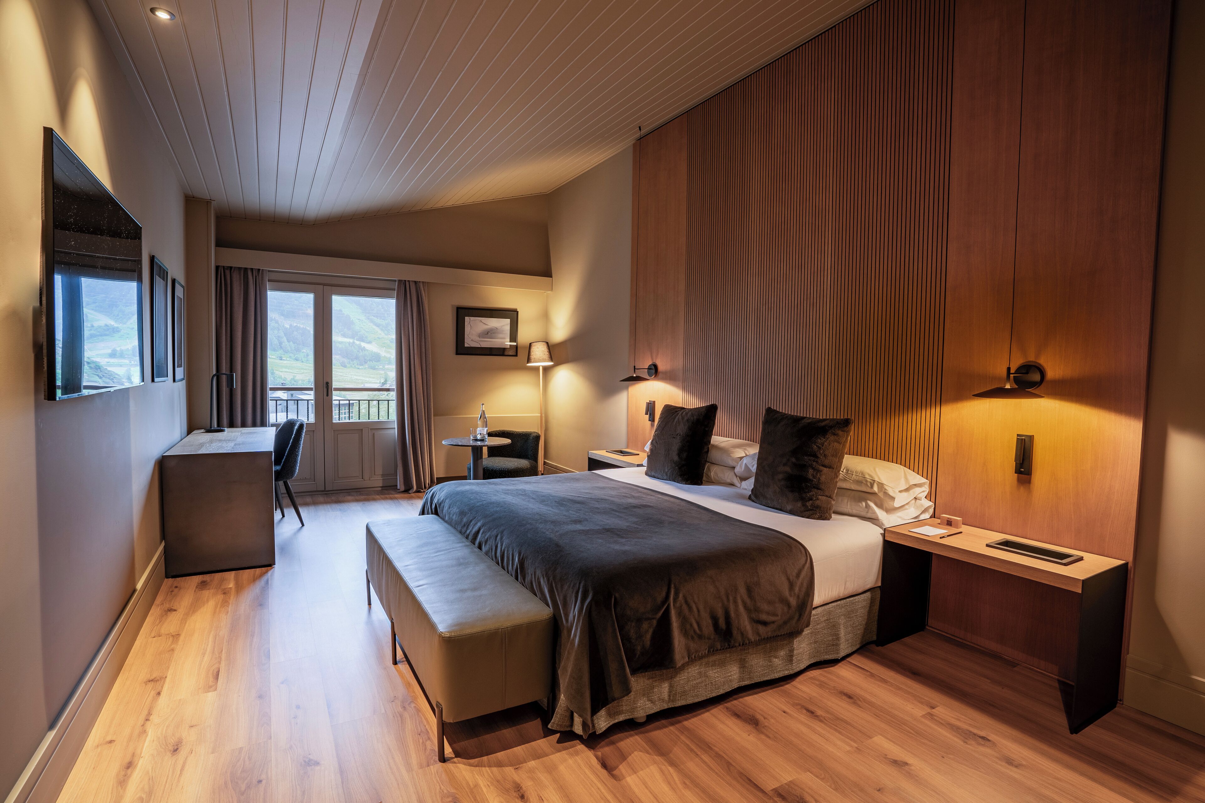 Quarto de hotel moderno com uma cama grande, uma escrivaninha, uma cadeira e vista para o exterior.
