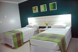 Quarto de hotel com duas camas, uma mesa de cabeceira com abajur e um painel com três quadros.