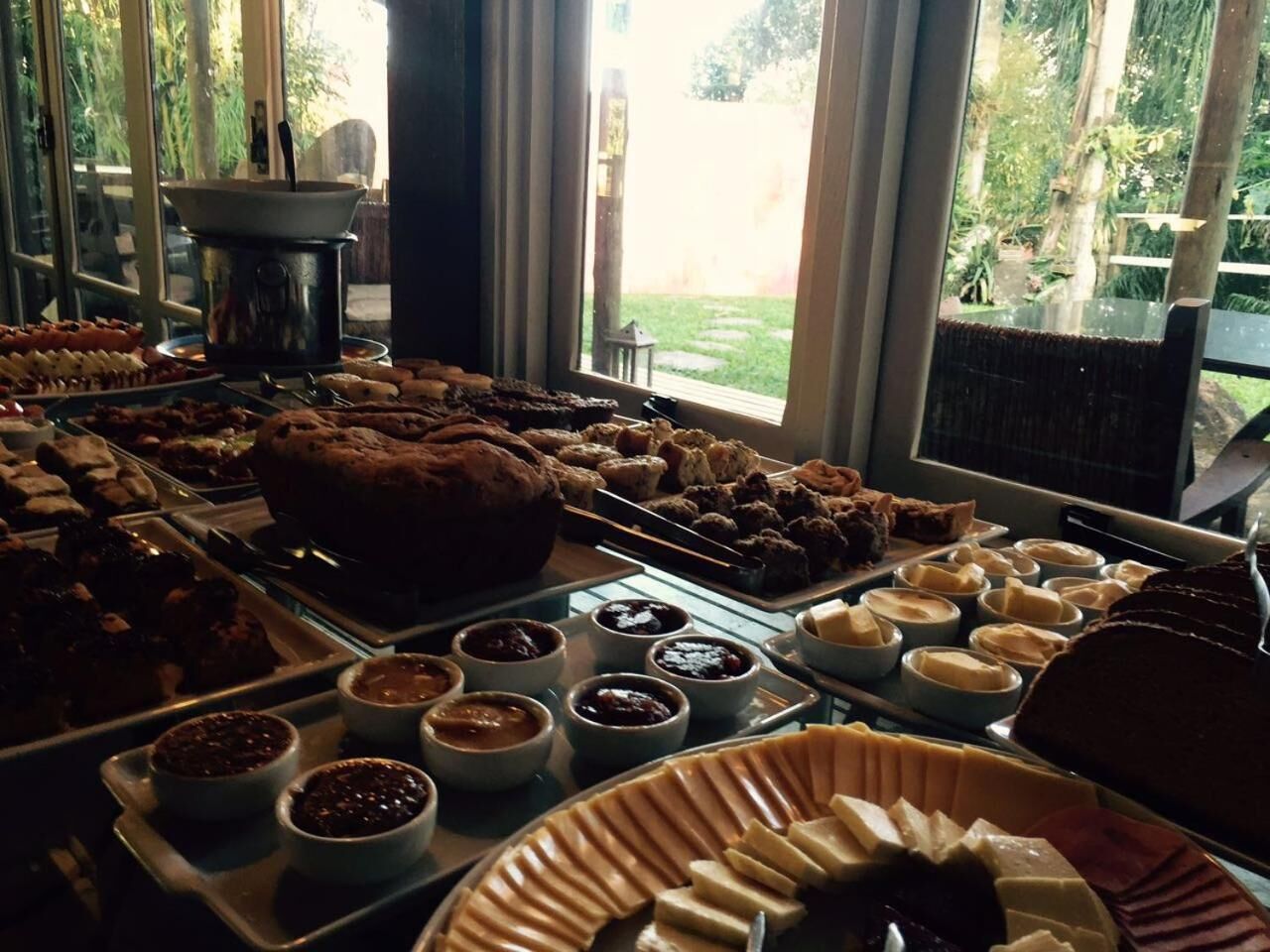 Buffet com diversos doces e patês, incluindo bolos, pastéis e molhos, dispostos em bandejas.