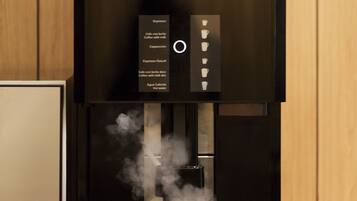 Máquina de café a soltar vapor, uma chávena e um menu sobre uma mesa de madeira.