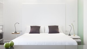 Quarto de hotel moderno com uma cama grande, duas mesas de cabeceira e um criado-mudo.